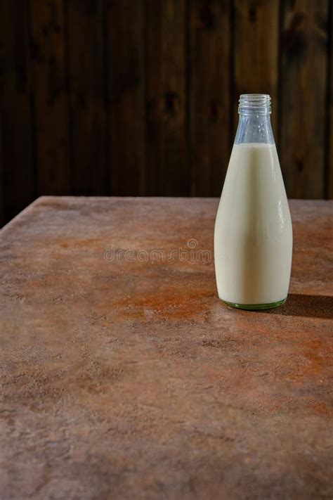 On A Textured Rusty Table In The Distance Stands A Beautiful Small Glass Bottle Of Milk