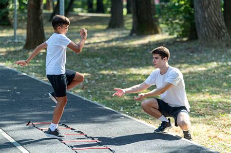 소년은 민첩성 사다리를 사용하여 트레이너와 함께 야외에서 운동합니다 이 세션은 전문가의 지도하에 재미있고 매력적인 환경에서 조정력 속도 및 체력을 촉진합니다 18 19세에