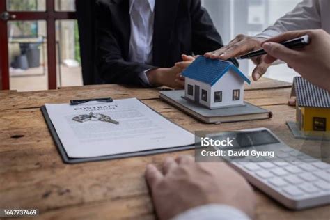 부동산 중개인은 모기지 대출 제안 및 주택 보험에 관한 의사 결정에 서명하고 보험 양식 계약 주택 모델 매매를 위해 고객에게 제시하고 상담합니다 2명에 대한 스톡 사진 및