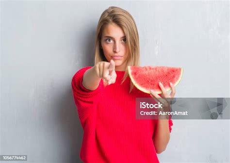 당신에 게 카메라를 손가락으로 가리키는 물 참 외를 먹는 그런 지 회색 벽에 아름 다운 젊은 여자 손 기호 정면에서 긍정적이 고 자신감 제스처 가리키기에 대한 스톡 사진 및