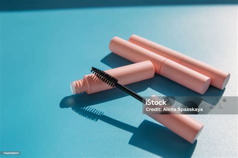 마스카라 용 핑크 클린 메이크업 브러시는 열린 튜브 닫힌 화장품 튜브 립글로스 액체 립스틱 그림자가있는 파란색 배경에 분홍색 아이 라이너 옆에 있습니다 복사 공간 마스카라에