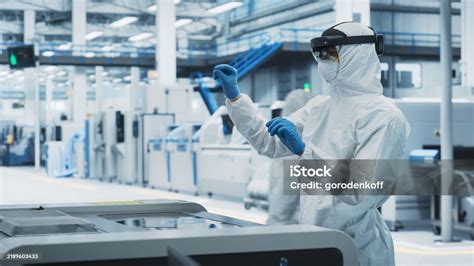 멸균 작업복 착용 엔지니어는 증강 현실 헤드셋을 사용하여 제조 시설의 실리콘 마이크로칩 모델 컴퓨터 하드웨어의 정밀 엔지니어링과