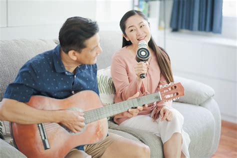 부부 선배 아시아는 은퇴 가정에서 기타를 연주와 함께 노래하고있다 은퇴 한 남자와 여자는 소파에 앉아 행복하게 벌채를 즐기고 웃는 재미를 음악을 연주하고 있습니다 가족에