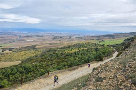 팜플로나 스페인 두 명의 순례자가 세인트 제임스의 길에서 팜플로나 근처의 알토 델 페르돈 에있는 순례자 그룹의 철 조각품에 접근합니다 산티아고 데 콤포스텔라에 대한 스톡