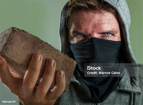 벽돌 돌을 들고 급진적이고 공격적인 무정부 주의자 리오터로 젊은 남자 회색 배경에 고립 된 폭력 시위에서 폭동과 싸우는 얼굴 마스크에 분노와 반 시스템 시위자