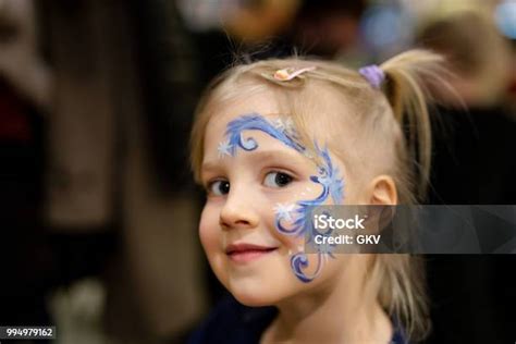 페이스 페인팅으로 귀여운 작은 금발 소녀 아이 얼굴에 수채화로 블루 추상 눈송이 패턴입니다 화려한 그림을 가진 사랑 스러운