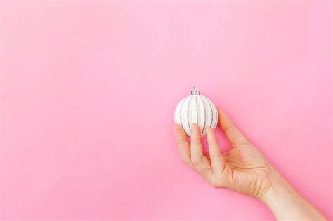 분홍색 파스텔 컬러의 트렌디 한 배경에 고립 된 크리스마스 장식 공을 들고 있는 최소한의 디자인 여성 12월에 대한 스톡 사진