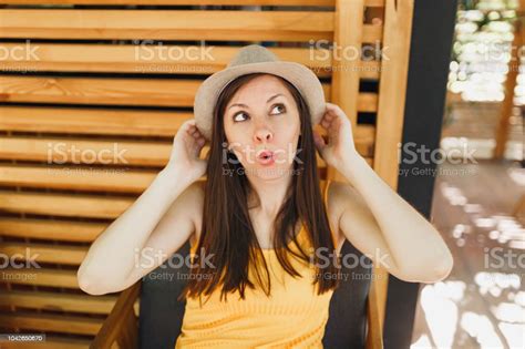 밀 짚 여름 모자 노란색 셔츠에에서 흥분된 웃는 젊은 여자의 초상화 야외 거리 여름 커피숍 카페에서 나무 바탕에 머리에 손을 넣어 사람들이 진심으 감정 라이프 스타일 개념