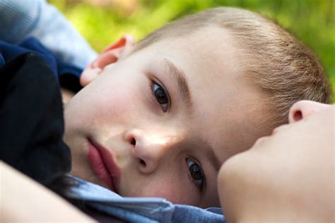 따뜻한 화창한 여름 날에 어머니 가까이에 녹색 잔디에 누워 회색 꿈꾸는 눈을 가진 귀여운 잘 생긴 아이 소년의 클로즈업 초상화 엄마와 아들 사이의 행복한 가족 관계 사랑과