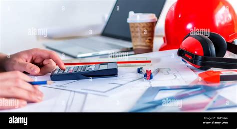 Closeup Of An Architect Calculating The Project Costs On A Desk Covered In Blueprints Stock