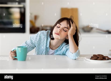 Sleepy young woman drinking coffee, feeling tired, suffering from insomnia and sleeping disorder ...