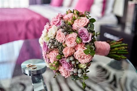 새틴 리본과 유리 테이블 배경에 흐릿한 두 개의 황금 반지와 분홍색과 보라색 장미의 무성한 신부 꽃다발을 닫습니다 공간을 복사 웨딩 컨셉 0명에 대한 스톡 사진 및 기타