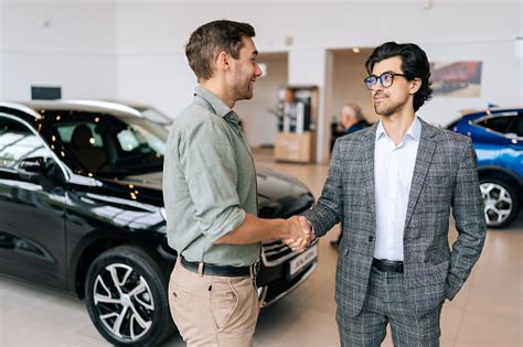 쇼룸에서 젊은 남자 고객을 환영하는 비즈니스 정장을 입은 자신감 넘치는 자동차 딜러의 초상화 자동차 대리점에서 고객과 악수하는 전문 세일즈맨 동의에 대한 스톡 사진 및 기타