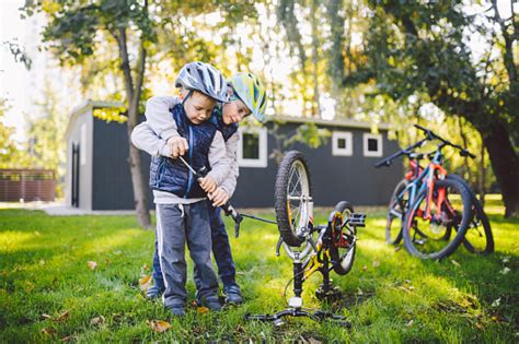 두 아이 오래 된 소년과 동생은 수리 자전거를 학습 두 남자 형제에 헬멧 및 단일 의류 사용 펌프 도구 및 펌프 공기 자전거 바퀴 공원에서 집의 배경 가족에 대한 스톡 사진