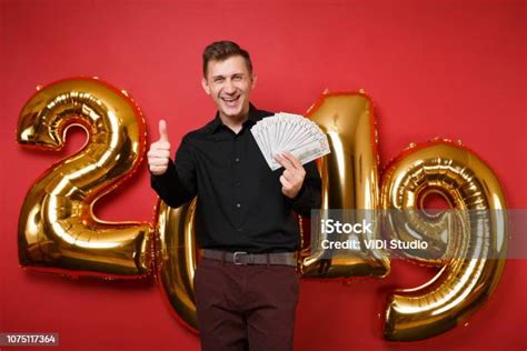 검은 셔츠 축 하 휴일 파티 현금 돈을 들고 있는 메리 젊은이 밝은 빨간 벽 배경 골든 번호 공기 풍선 스튜디오 초상화에 고립 행복 한 새 해 2019 크리스마스 개념입니다