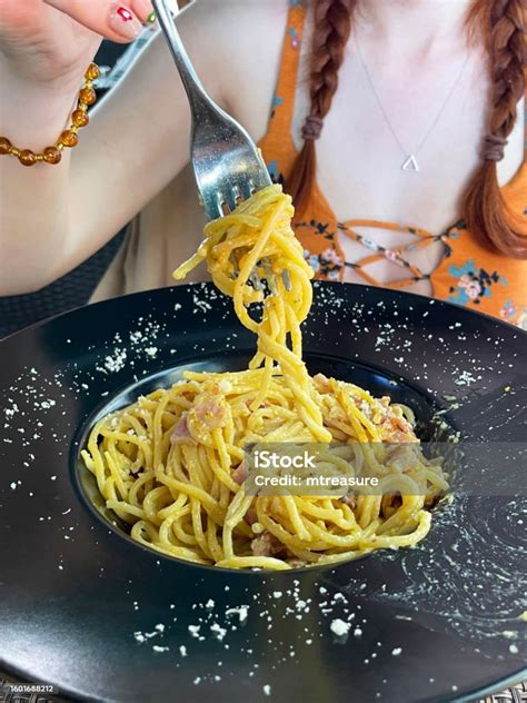 금속 포크 검은 접시 구타 계란 베이컨 이탈리아 파마산 치즈와 마늘을 곁들인 까르보나라 소스에 스파게티 더미 레스토랑 장면 배경 전경에 초점을 맞춘 알아볼 수 없는 사람의