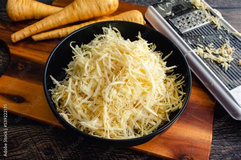 Bowl Of Shredded Parsnips On A Wood Cutting Board Whole And Shredded