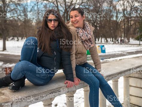 Two Girls Hanging Out In The Park Sitting On A Railing And Having Fun