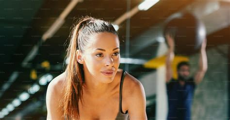 포니테일과 긴 갈색 머리를 가진 아름다운 백인 여성이 체육관에서 필라테스 공으로 운동을 하고 있습니다 필라테스 공을 가진 남자의 배경 반영 사진 Unsplash의