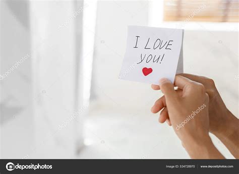 unrecognizable woman putting sticky note with i love you text on mirror