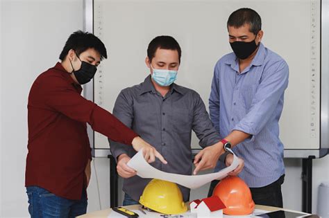 사무실에서 함께 일하는 보호 마스크를 착용한 건축가와 엔지니어의 자신감 있는 팀 그들은 책상에서 새로운 시작 프로젝트에 대해