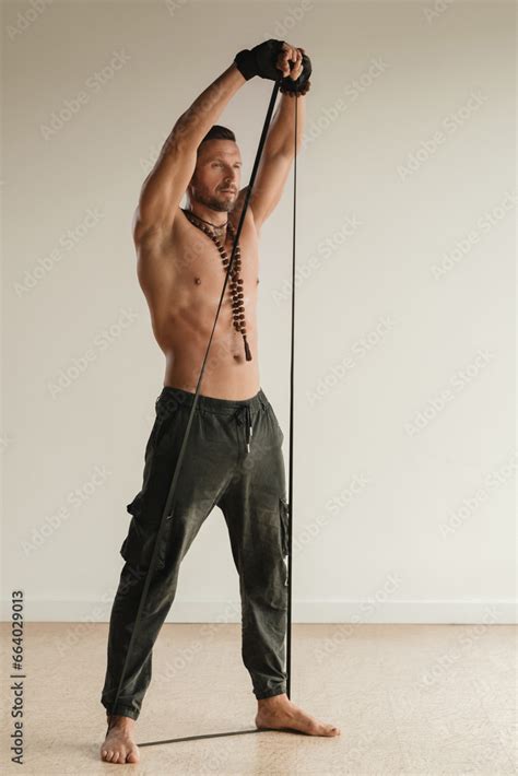A Man With A Naked Torso Is Engaged In Strength Fitness Using A Rubber