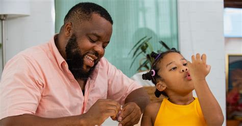 행복한 가족 아프리카 아버지는 거실에서 어린 딸에게 매니큐어를 바르고 있다 아빠와 여자 아이는 집에서 미용 치료와 함께 즐거운