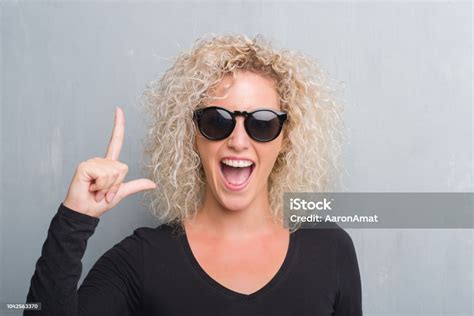 그런 지 회색 배경에 성공적인 아이디어와 손가락 가리키는 곱슬 머리를 가진 젊은 금발 여자 종료 하 고 행복 번호 하나입니다 가리키기에 대한 스톡 사진 및 기타 이미지