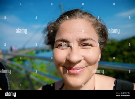 A Joyful Woman Squints And Smiles Warmly Under The Bright Sunlight At The Langkawi Sky Bridge In