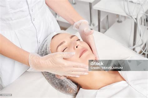미용사는 클리닉에서 회춘을 위해 보습 크림을 문지른 후 여성의 얼굴 피부를 마사지합니다 30 34세에 대한 스톡 사진 및 기타 이미지 30 34세 건강관리와 의술