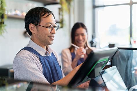 일본인 시니어 커피 숍 주인은 레스토랑의 카운터 바에서 커피 잔에 고객 이름을 쓰는 바리 스타와 함께 계산원의 음식 및 음료 주문과 터치 스크린을받습니다 개수대에 대한 스톡