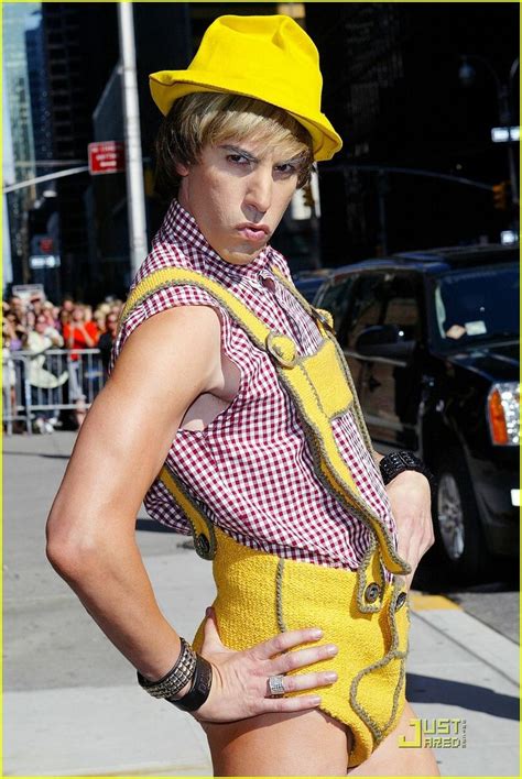 A Woman Wearing A Yellow Hat And Overalls On The Street With Her Hands