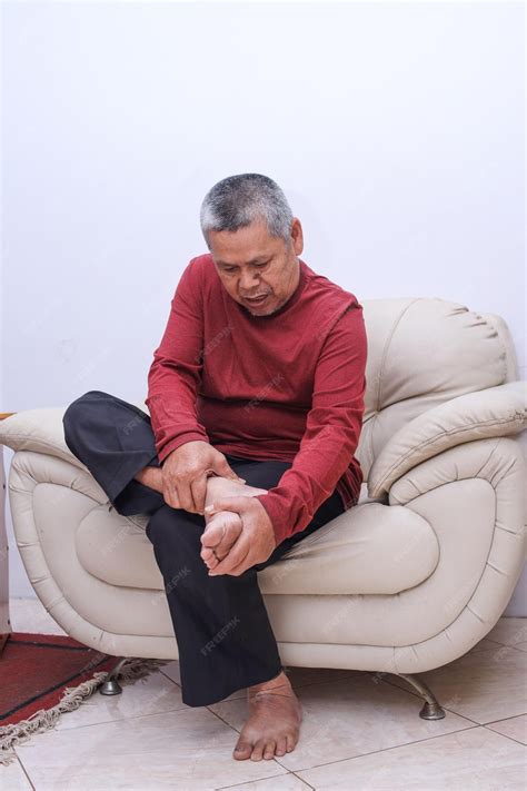 Premium Photo Elderly Asian Man Massaging His Aching Feet With His Hands While Sitting On The