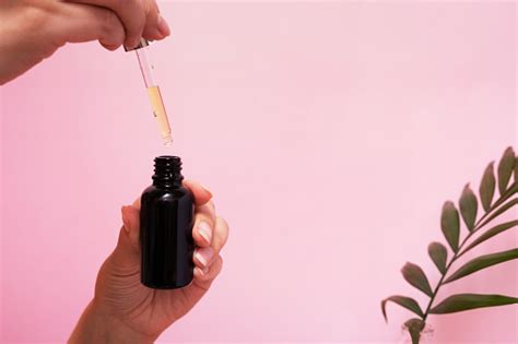 여성 손에 점적기 병에 화장품 오일 스파와 뷰티 테라피 야자수 잎 장식이있는 분홍색 배경 방울에 대한 스톡 사진 및 기타 이미지 Istock