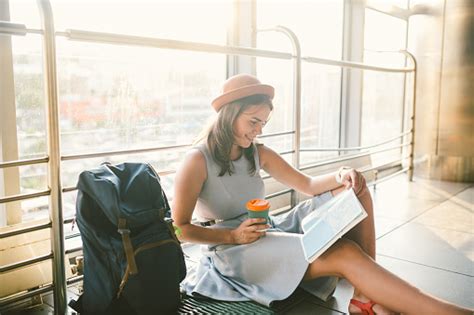 대기 공항 또는 기차역의 터미널에서 전송 지연 드레스와 모자에 젊은 백인 여자는 객실에 창 근처 배낭 관광 양탄자에 앉아 관광 지도로 본다 개념에 대한 스톡 사진 및 기타