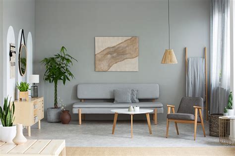 현대 포스터 방석과 라운지 안락의 자 나무 커피 테이블 및 밀 짚 램프 회색 거실 인테리어의 실제 사진 밀짚에 대한 스톡 사진