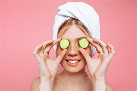 분홍색 배경에 그녀의 눈 근처 오이 조각을 들고 수건으로 그녀의 머리에 감싸 매력적인 쾌활 한 여자 가꿔주기에 대한 스톡 사진 및 기타 이미지 Istock