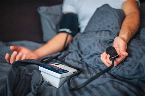 몸의 덮여 낮은 부분과 나쁜에 누워 남자의 절단 보기 그는 혈압을 측정 하기 위한 장치를 사용 합니다 그는 손에 압박을 위한 물건을 보유 하 고 있습니다 감기와 독감에 대한