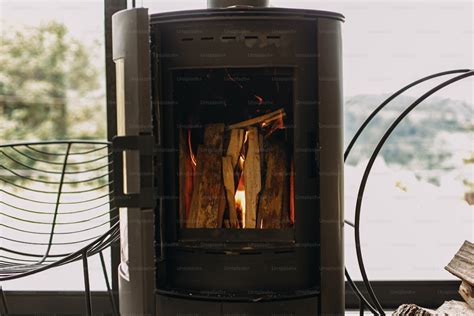 큰 창문을 배경으로 불타는 불과 금속 장작이 있는 현대적인 검은 벽난로 추운 계절에 아늑하고 따뜻하고 차분한 순간 오두막의 히터 사진 Unsplash의 굴뚝 이미지