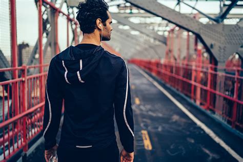 브릿지 서딩 운동에 서있는 스포츠웨어 라벨의 브랜드 이름이 있는 트랙수트를 입은 현대 이어폰의 핏 맨의 뒷모습 윈드 브레이커