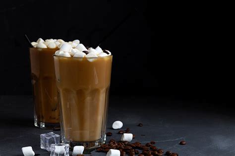 크림과 초콜릿 키 큰 유리에 마시멜로를 곁들인 맛있는 아이스 커피 검은 테이블에 커피 원두와 얼음으로 차가운 음료를 마셔야합니다 복사 공간이있는 검은 배경에 차가운 여름