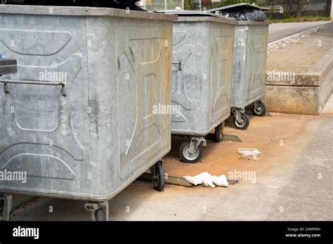 Three Trash Containers On Wheels With Trash Left Carelessly In Front Of