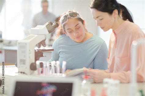 Female Teacher And Girl Babe Conducting Scientific Experiment At Microscope In Laboratory