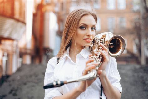 Молодая привлекательная девушка в белой рубашке при саксофон стоя в улице внешней Сексуальная