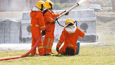 소방관은 화재 호스 화학 물 거품 스프레이 엔진을 사용하여 화염과 싸우고 소방관은 하드 모자 보호를위한 바디 안전 정장 유니폼을 착용합니다 소방 소화기 구조 훈련 건물