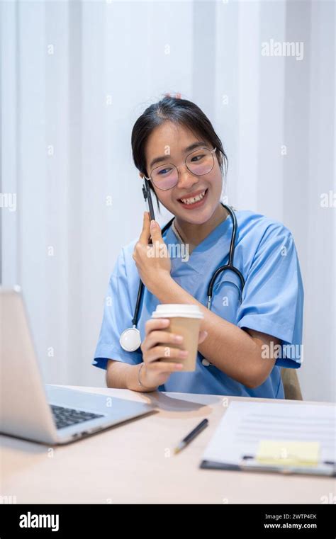 A Positive Hardworking Asian Female Doctor Is Multitasking Talking On The Phone With Someone