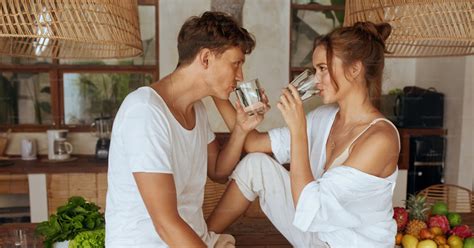 부엌에서 물을 마시는 낭만적인 커플 아름다운 여자와 잘생긴 남자가 나무 탁자에 앉아 서로를 바라보고 있다 트로피컬 빌라에서 여름 방학에 건강한 식단과 수분 공급 사진