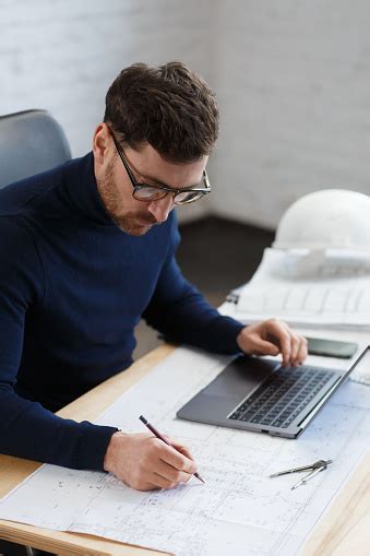 청사진이 있는 사무실에서 일하는 건축가 엔지니어가 건설 프로젝트를 스케치하여 건축 계획을 검사합니다 직장에 앉아 잘 생긴 수염 남자의 초상화 비즈니스 건설 개념 갈색 머리에