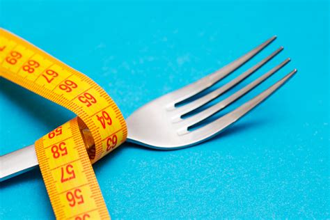 다이어트에 대 한 개념으로 포크 주위 테이프 측정 포크는 파란색 배경에 노란색 측정 테이프로 싸여 가냘픈에 대한 스톡 사진 및 기타 이미지 Istock