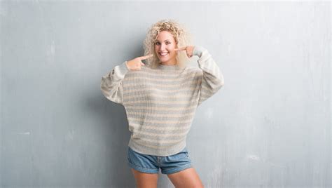 그런 지 회색 배경에 보여주는 자신감과 가리키는 손가락 치아와 입으로 웃 고 곱슬 머리를 가진 젊은 금발 여자 건강 개념입니다 미소에 대한 스톡 사진 및 기타 이미지